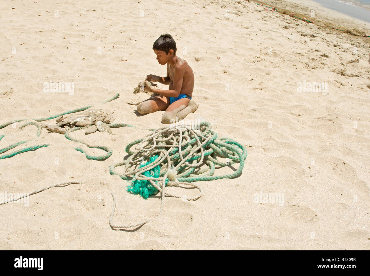 Boy sitting on beach removing sand from fish Stock Photo - Alamy
