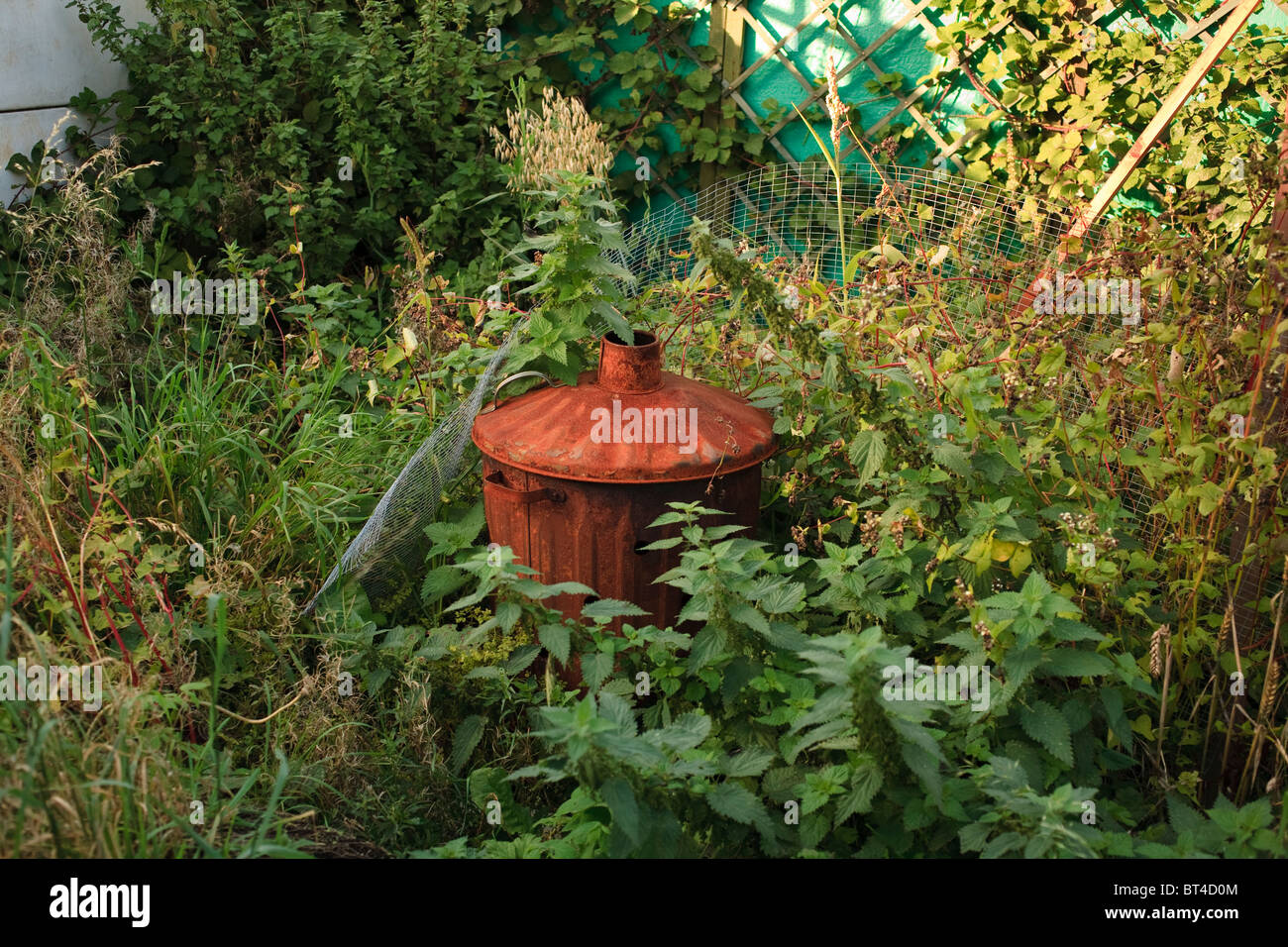 AN OLD RUSTED BIN/CHIMNEY INCINERATOR IN AN OVERGROWN GARDEN Stock ...