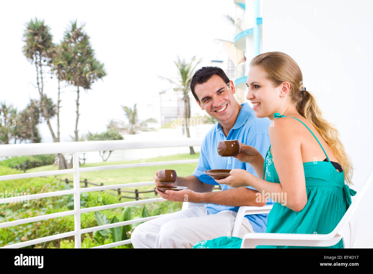 happy young couple sitting on balcony drinking coffee with beautiful ...