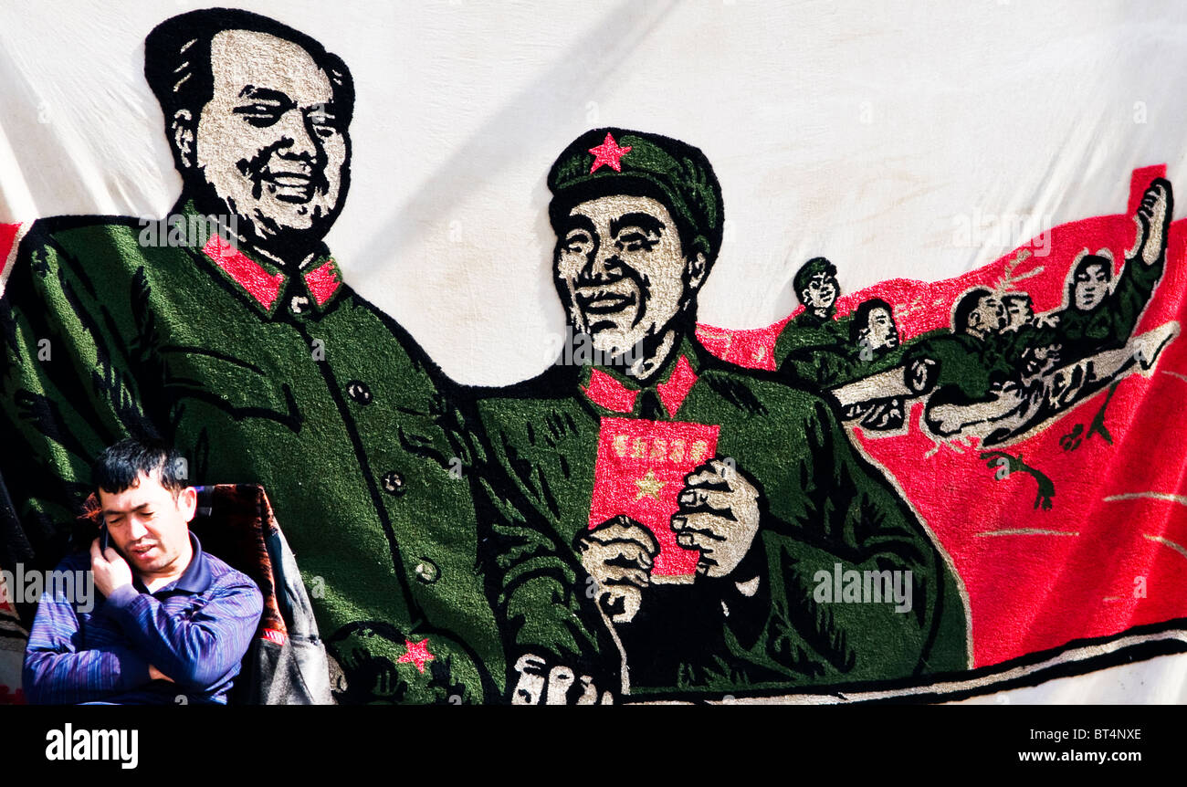 Chatting on his mobile phone by a big photo of his Communist heroes ...