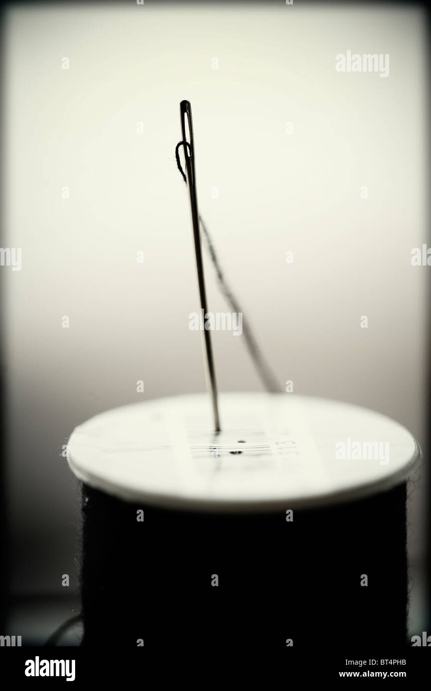 Black and white picture of a spool of black thread with threaded needle ...