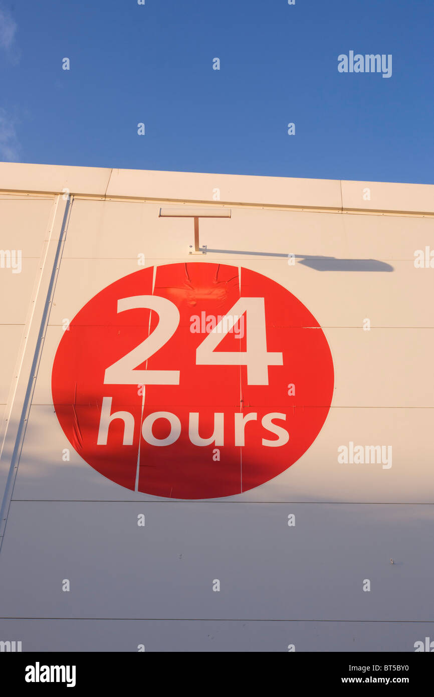Red circular sign telling shoppers that supermarket is open 24 hours a ...
