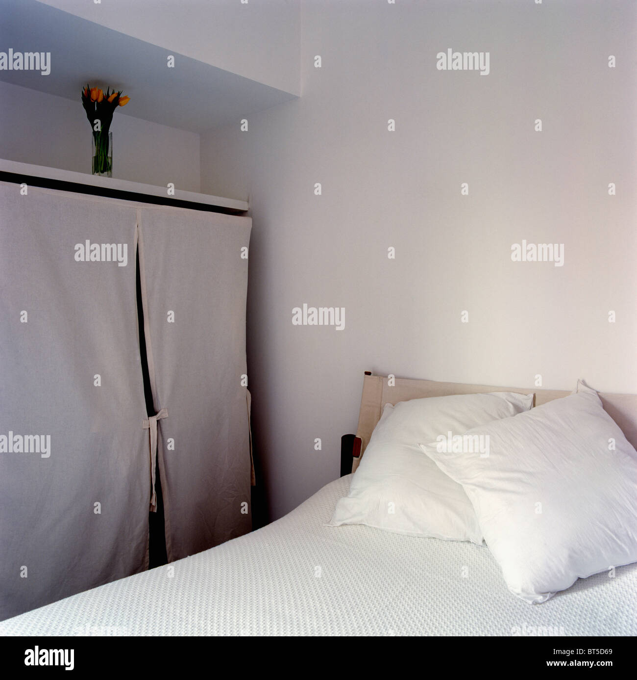 White tented wardrobe in alcove beside bed with white linen in economy ...