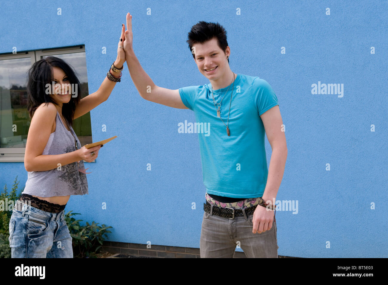 Happy teenagers outside school doing a high five after opening exam ...