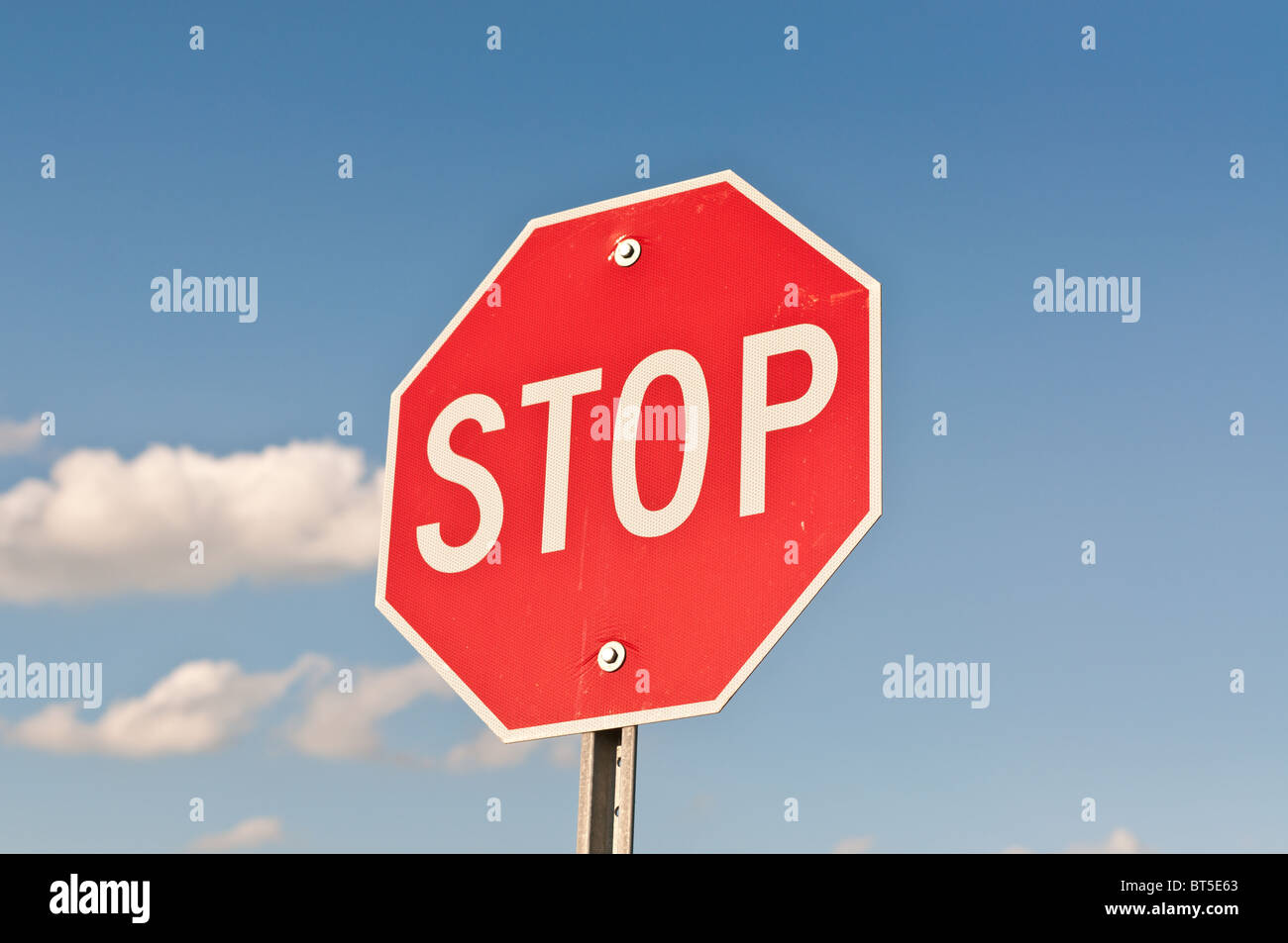 A red octagonal stop sign with blue sky and clouds in the background ...