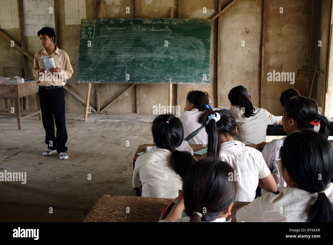 A male teacher is teaching his students by reading a Lao language book ...