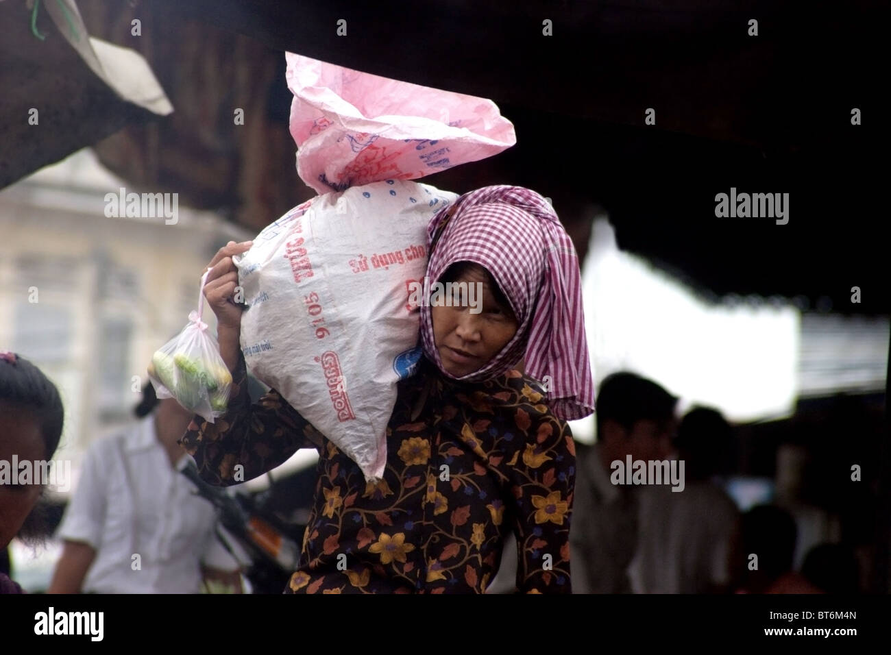 A Khmer woman is carrying a large and heavy sack of rice on her ...