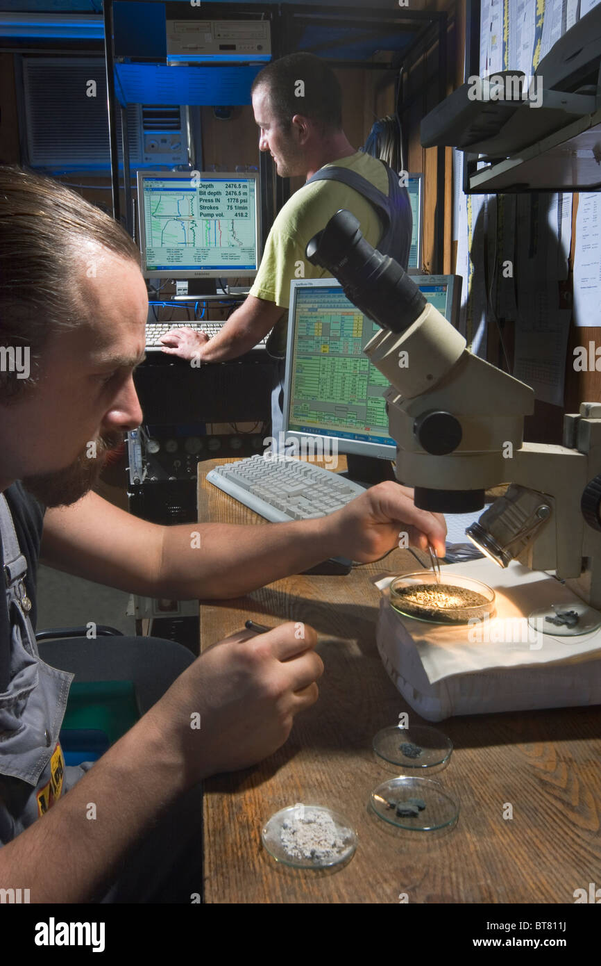 Mud loggers examining rocks and sediment inside mobile logging room ...