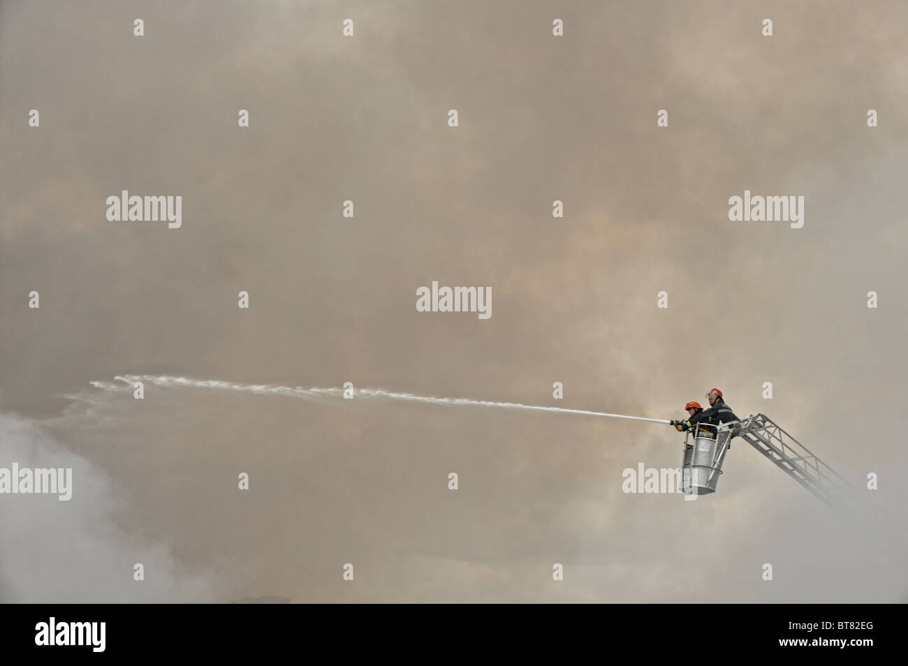 Firemen on a extension ladder fighting a massive factory fire amidst ...