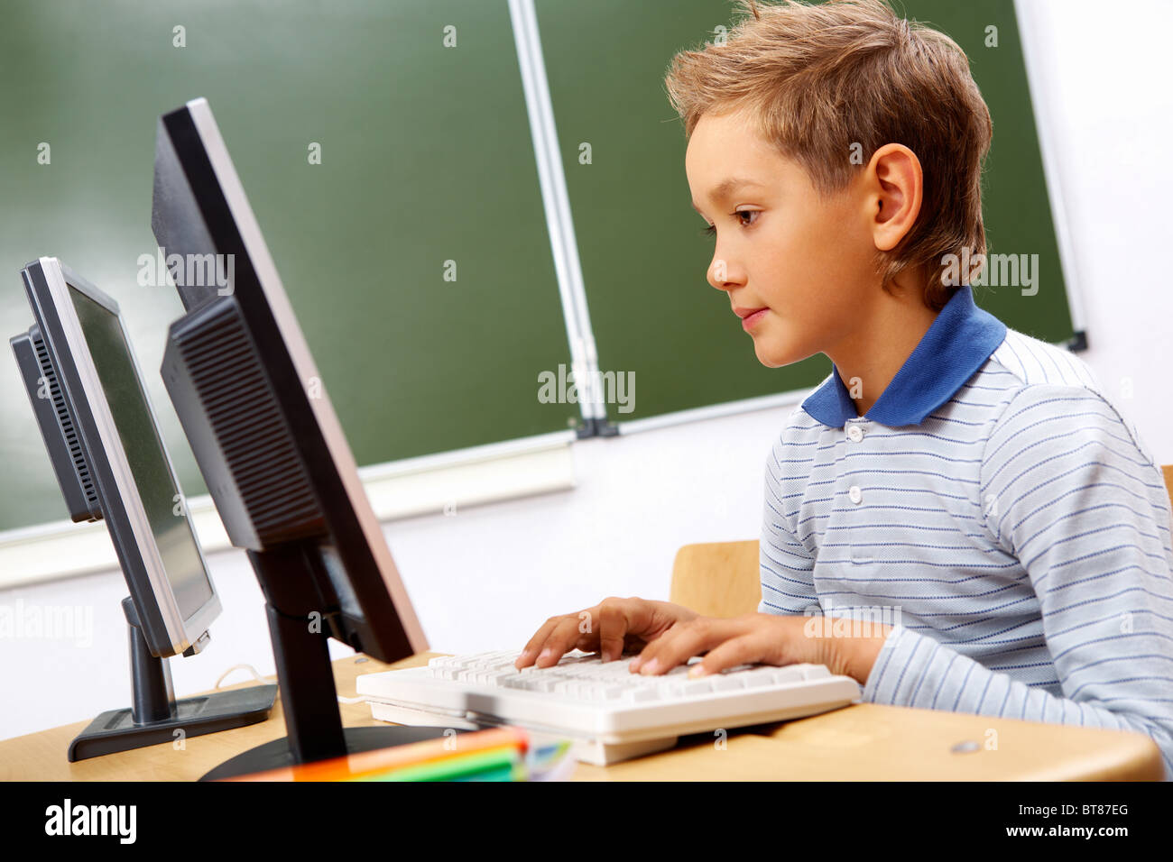 Portrait of cute lad typing on computer board in classroom Stock Photo ...