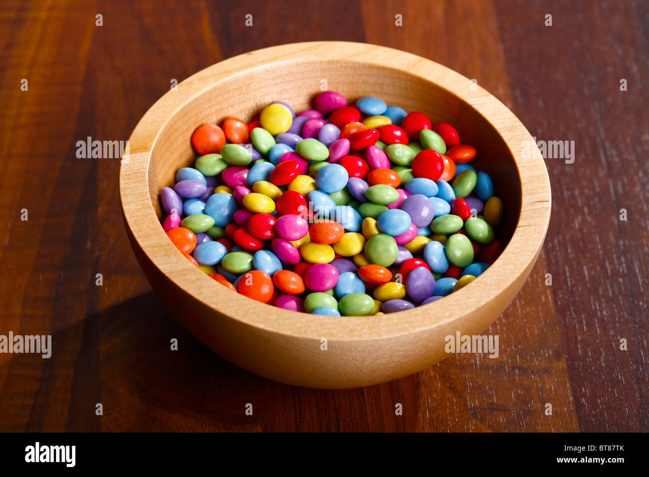 Coloured chocolate beans in wooden bowl on wooden table Stock Photo - Alamy
