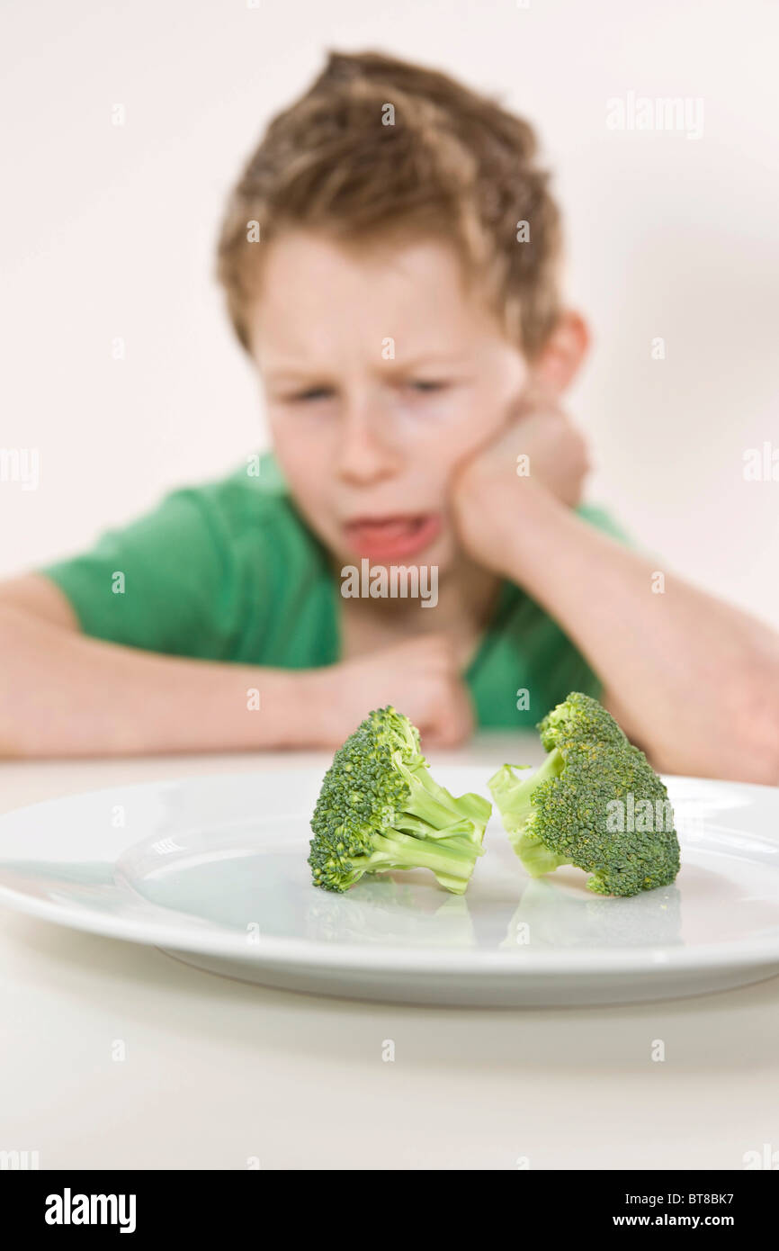 Boy sitting in front of a plate of broccoli with a disgusted look on ...
