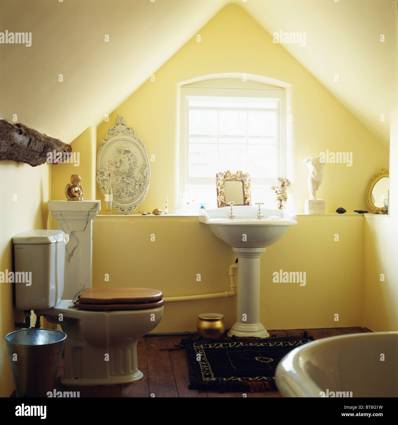 White pedestal basin below window in pale yellow attic country bathroom ...