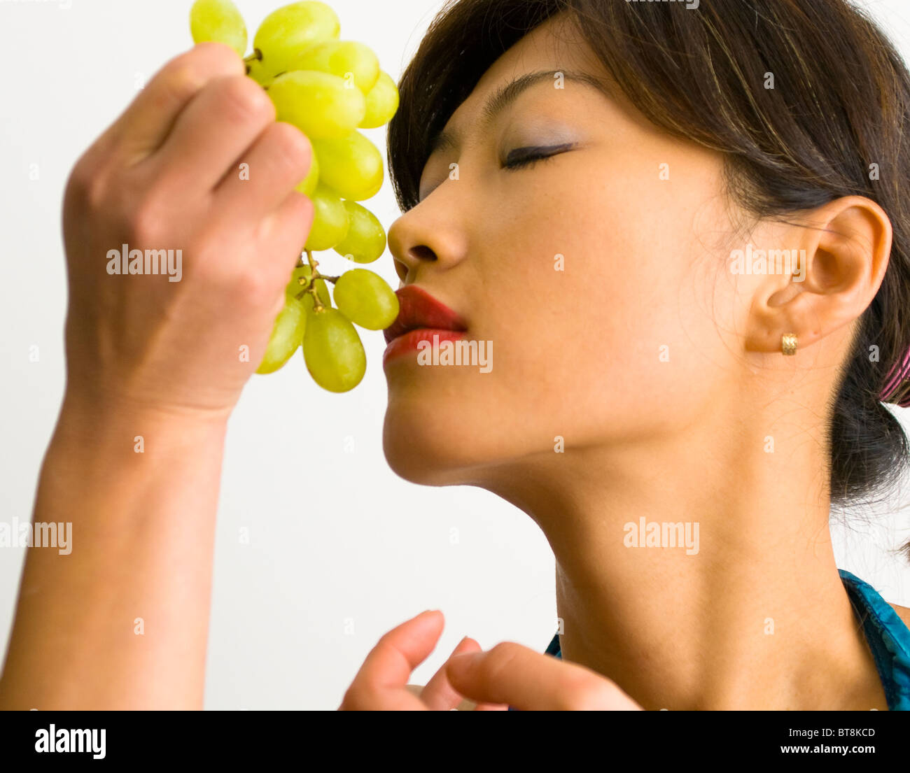 Young woman holding bunch of grapes to mouth with eyes shut Stock Photo - Alamy