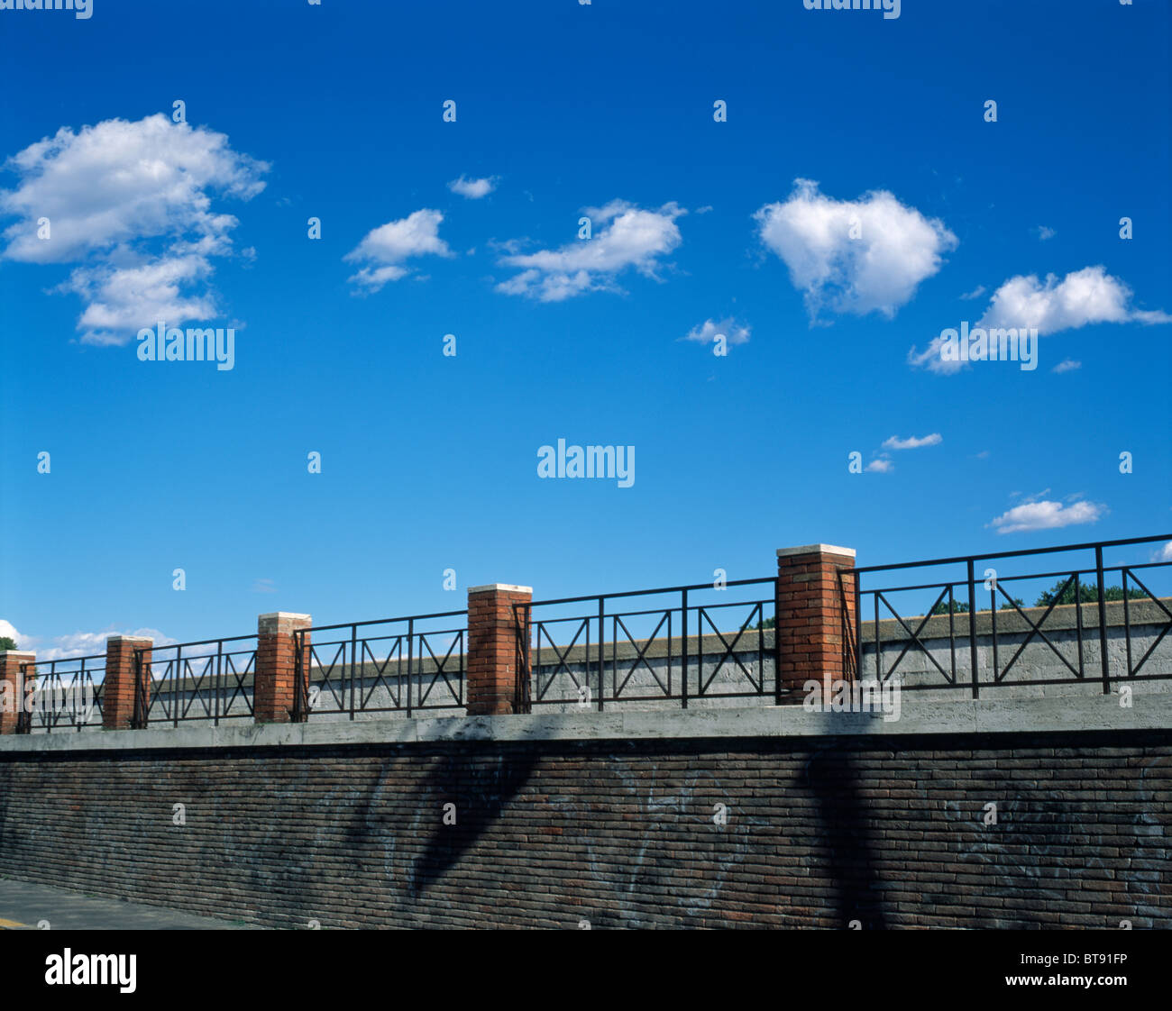 White clouds in blue sky and brick wall with railing in the foreground ...