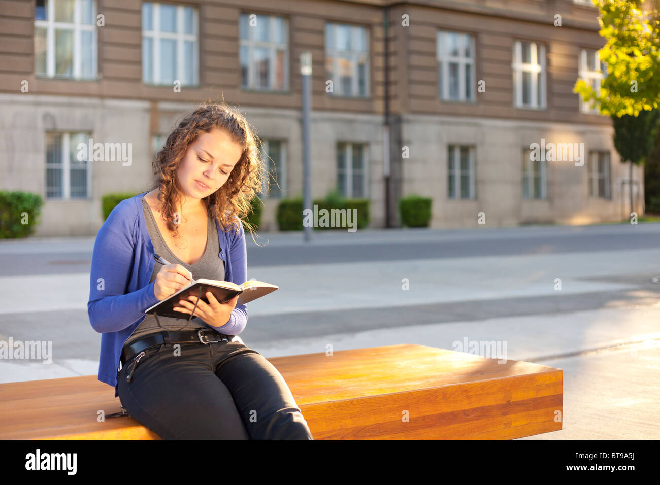 Young woman sitting on a bench writing in a notebook Stock Photo - Alamy