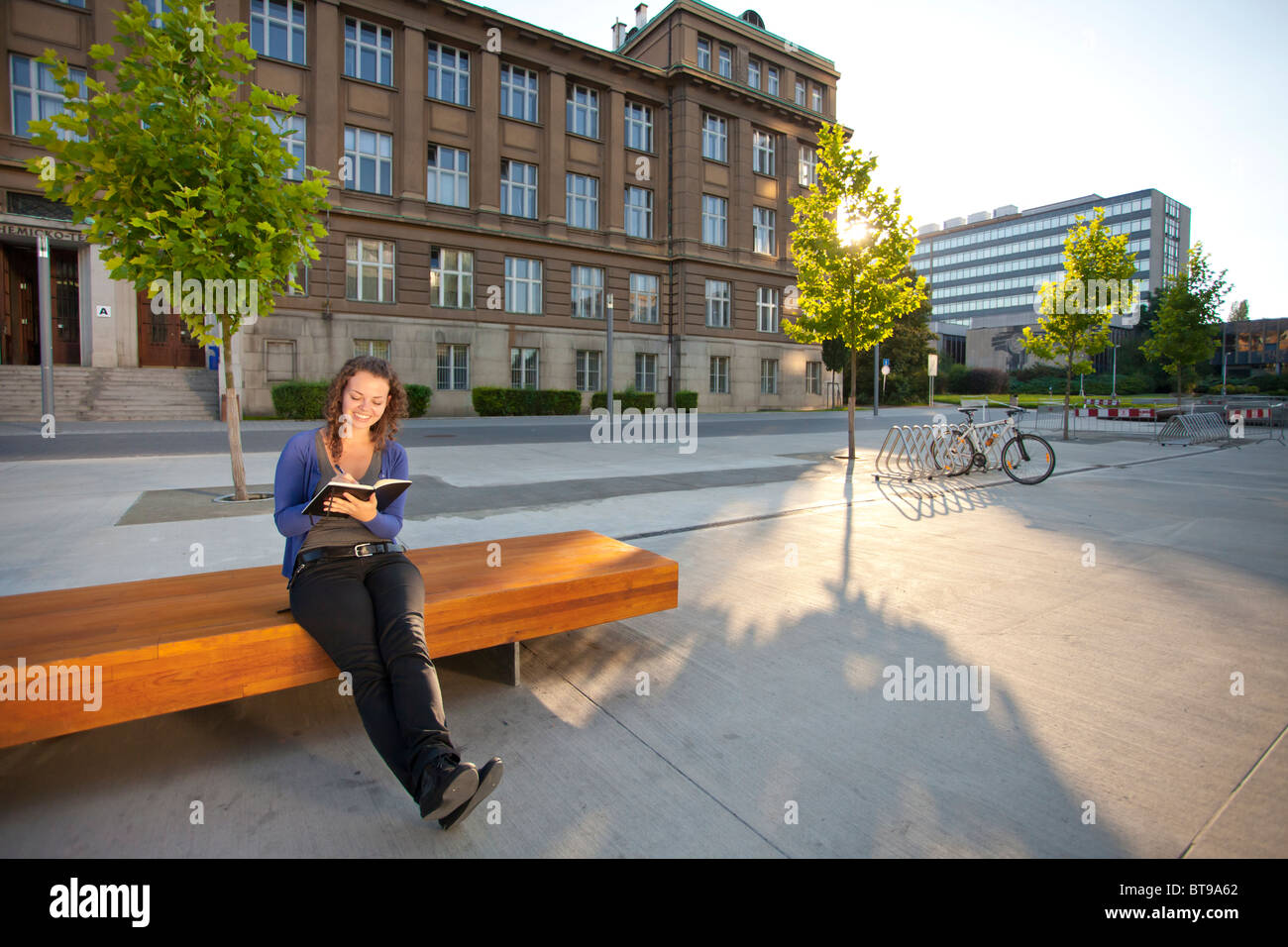 Young woman sitting on a bench writing in a notebook Stock Photo - Alamy