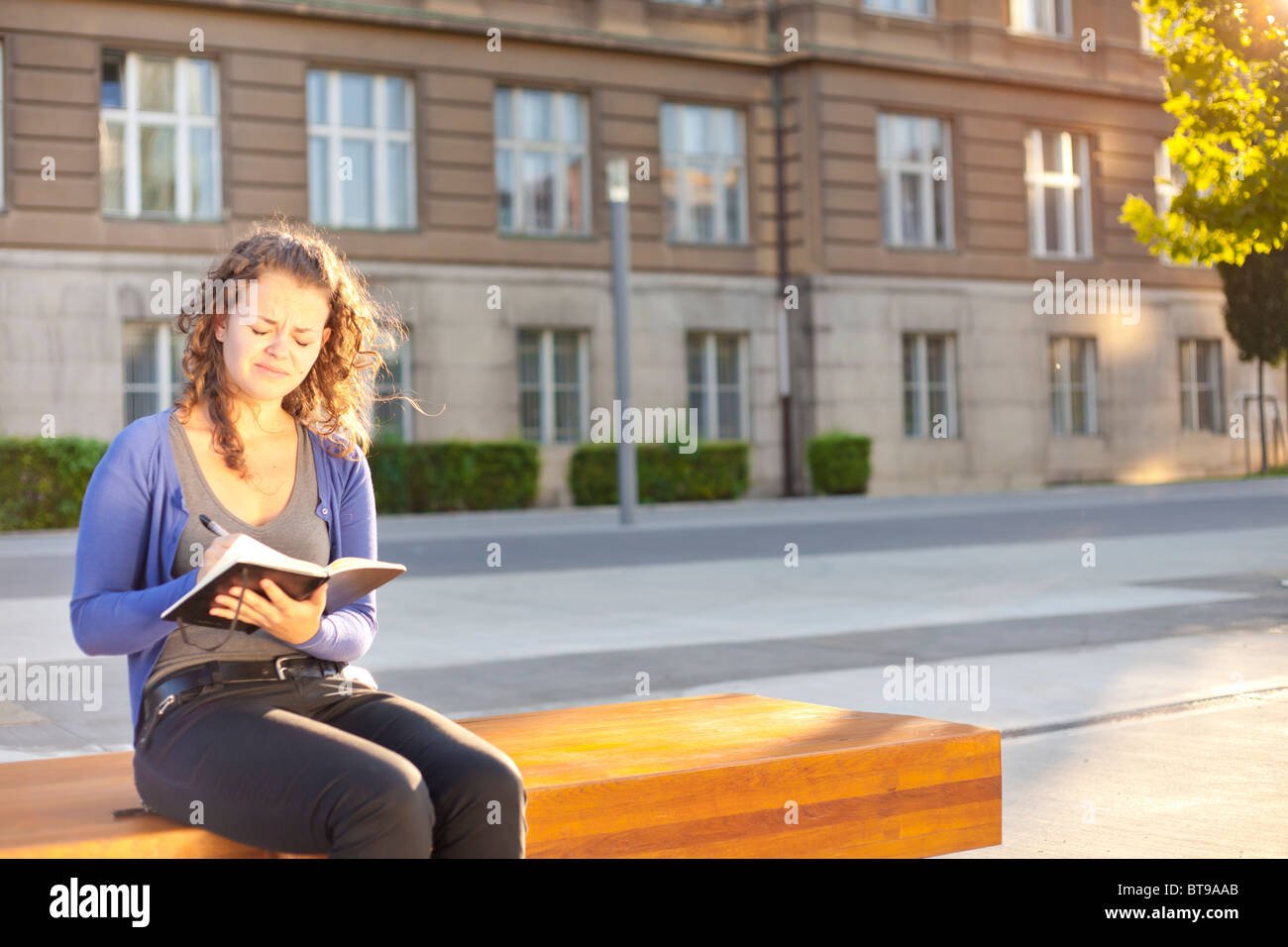 Young woman sitting on a bench writing in a notebook Stock Photo - Alamy