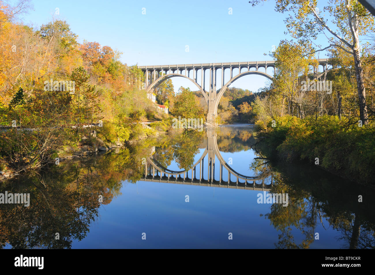 A high arched bridge reflected in a deep blue river in autumn Stock ...