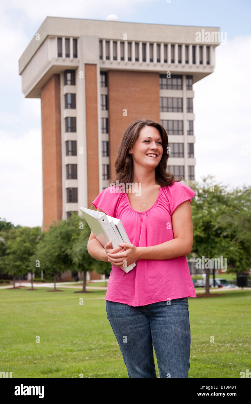 Female college student standing in front of school with books in hand ...