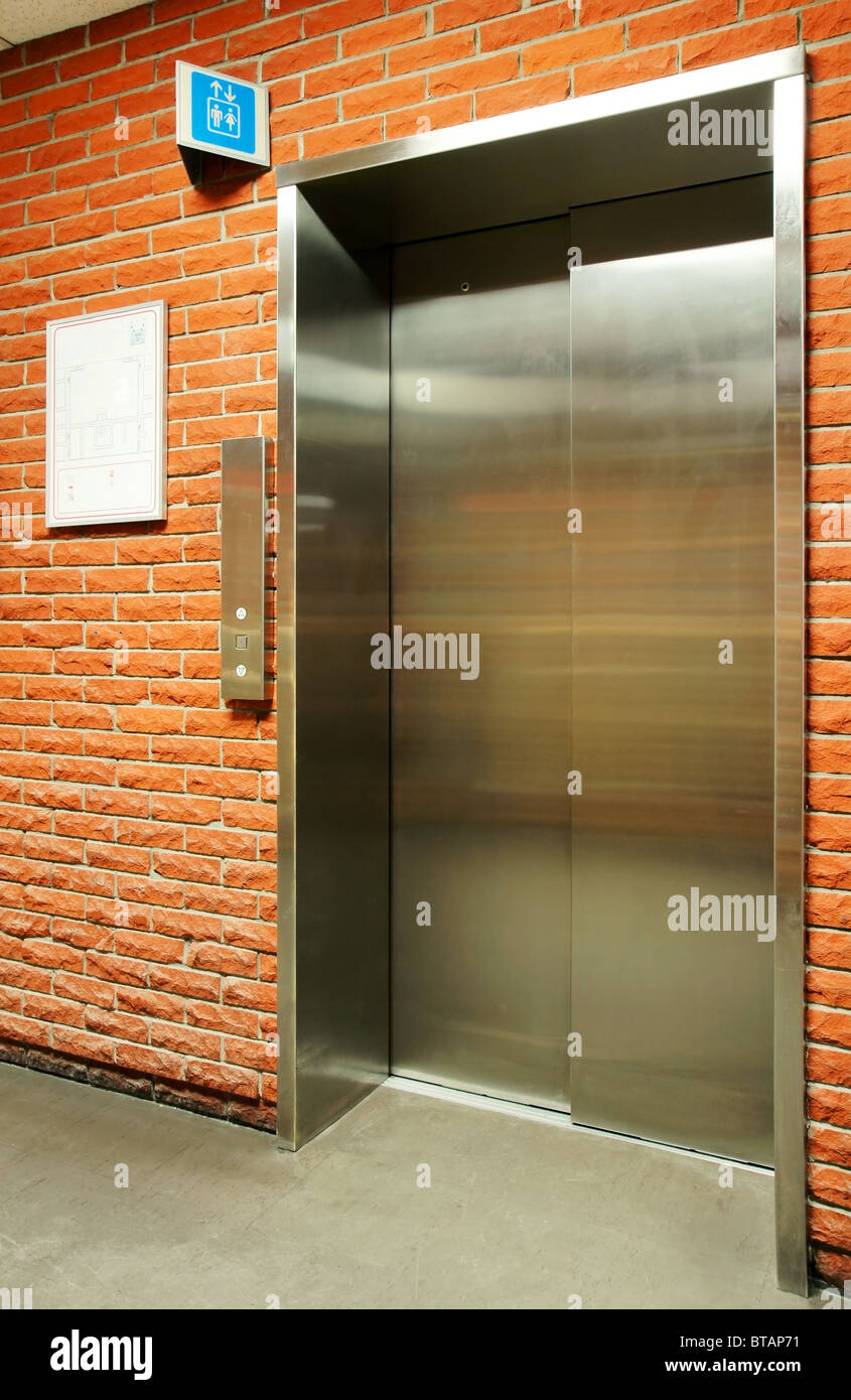 Vertical of closed steel door elevator in orange brick wall with blue ...