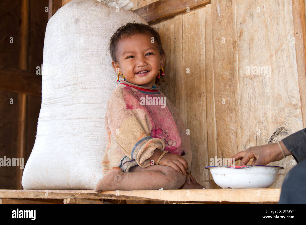 A happy Eng (Ann) minority girl sits on the porch while her sister ...