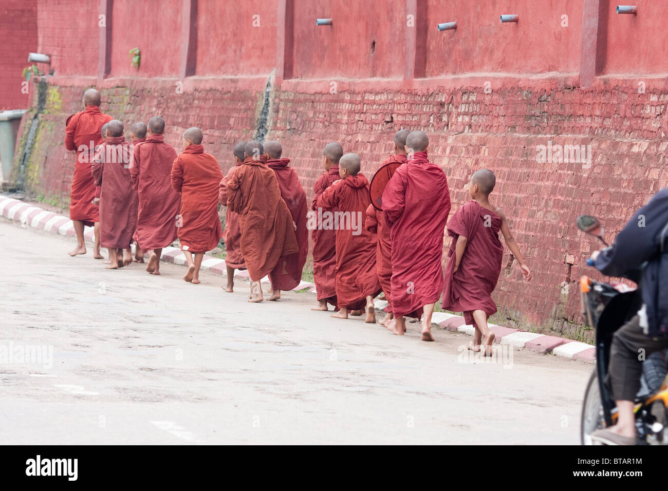 Monks and novice monks walk past a large red wall during their morning ...