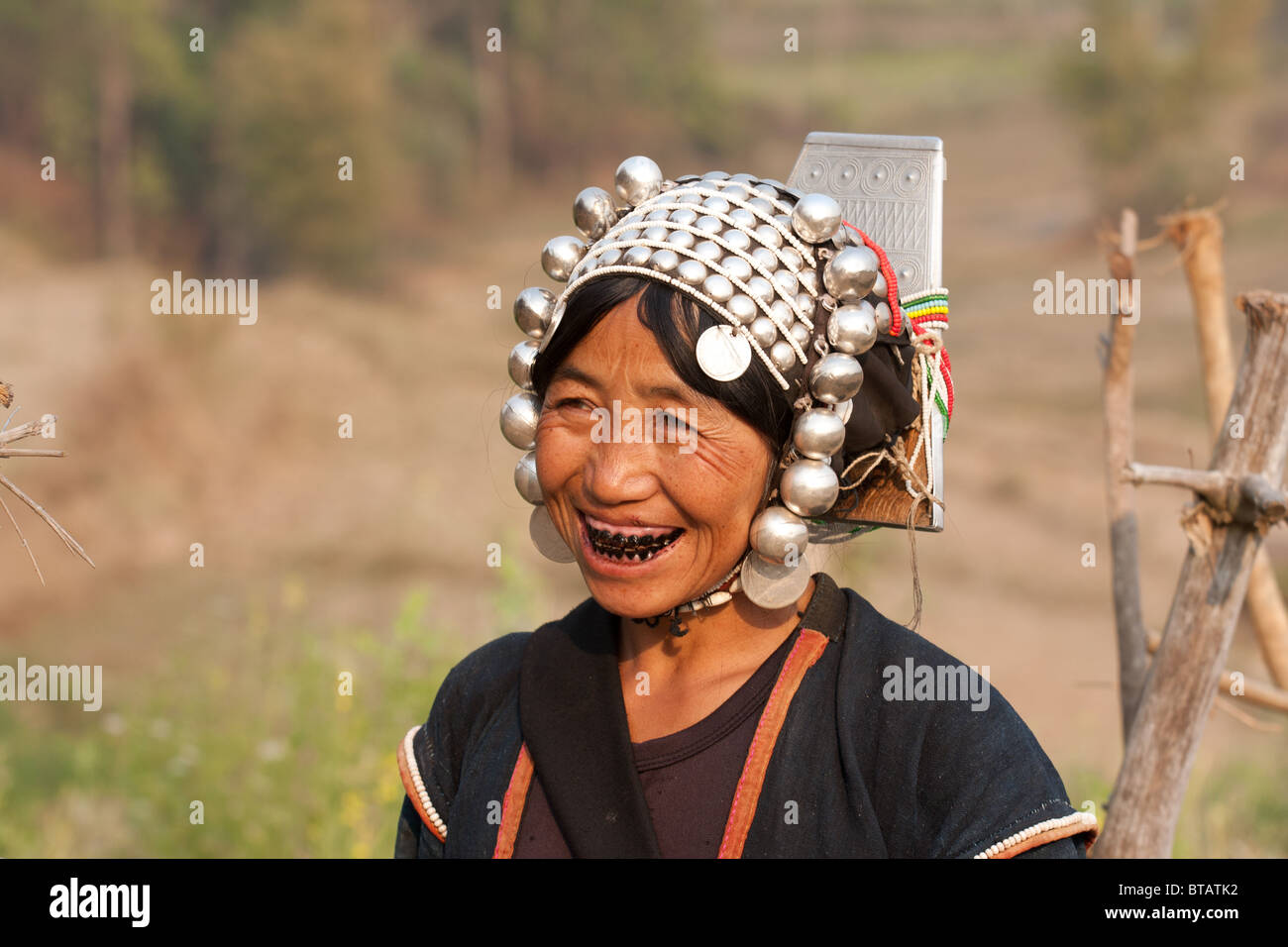 A smiling Akha woman with Blackened teeth wearing a traditional silver ...