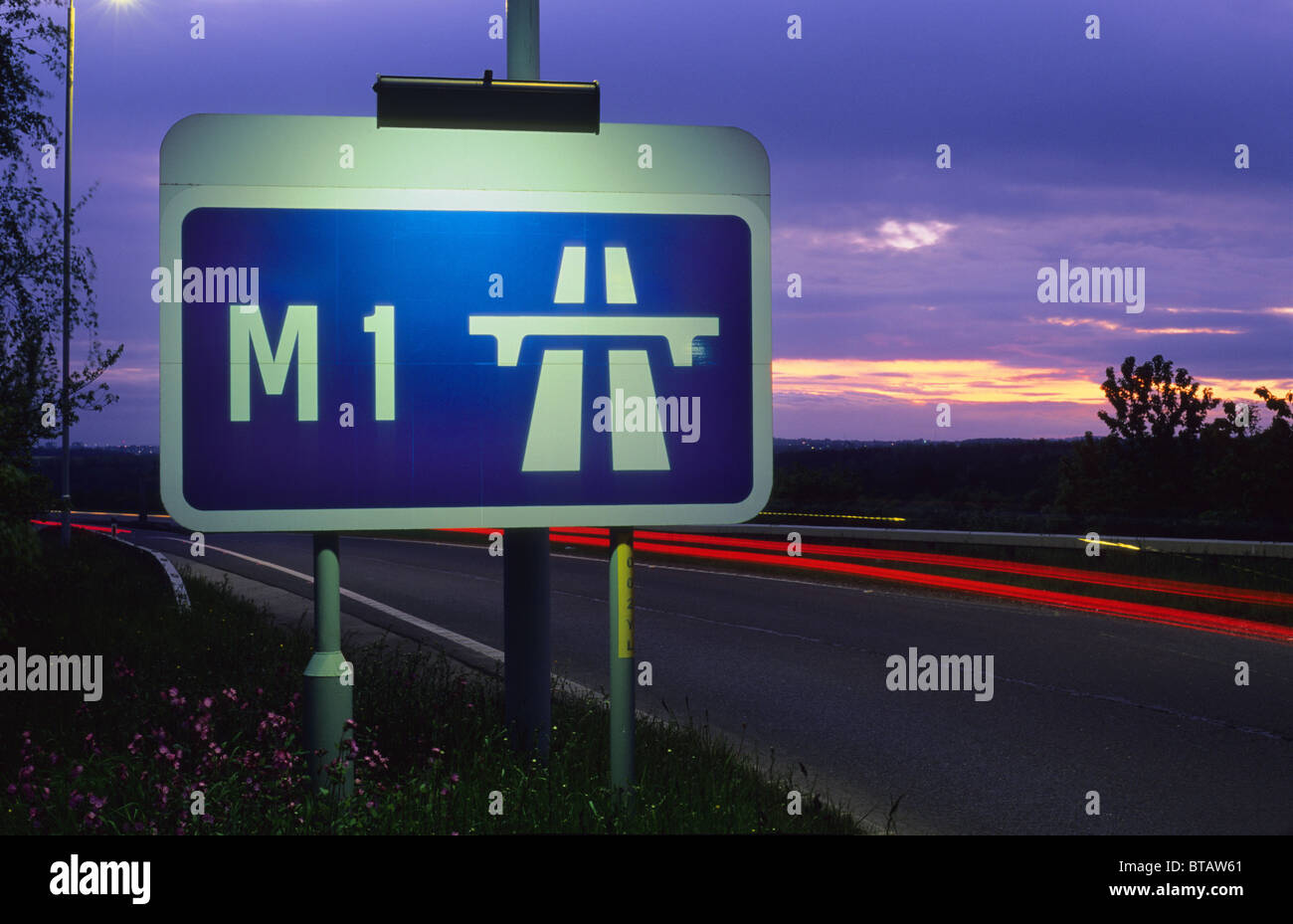 headlight trails of traffic passing M1 motorway sign at sunset near ...