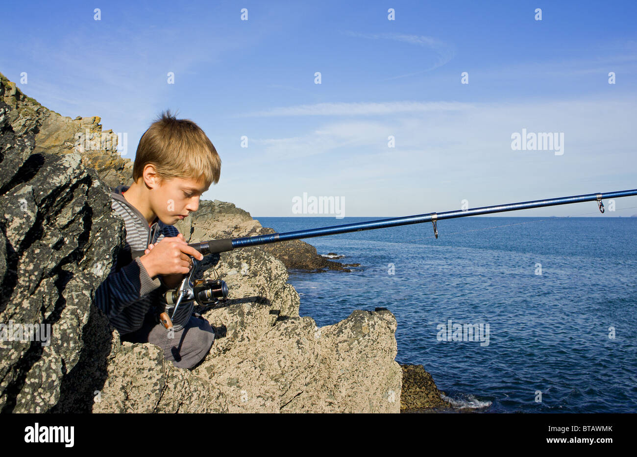 a young boy fishing from the rocks on Holy island, Angelsey. North ...