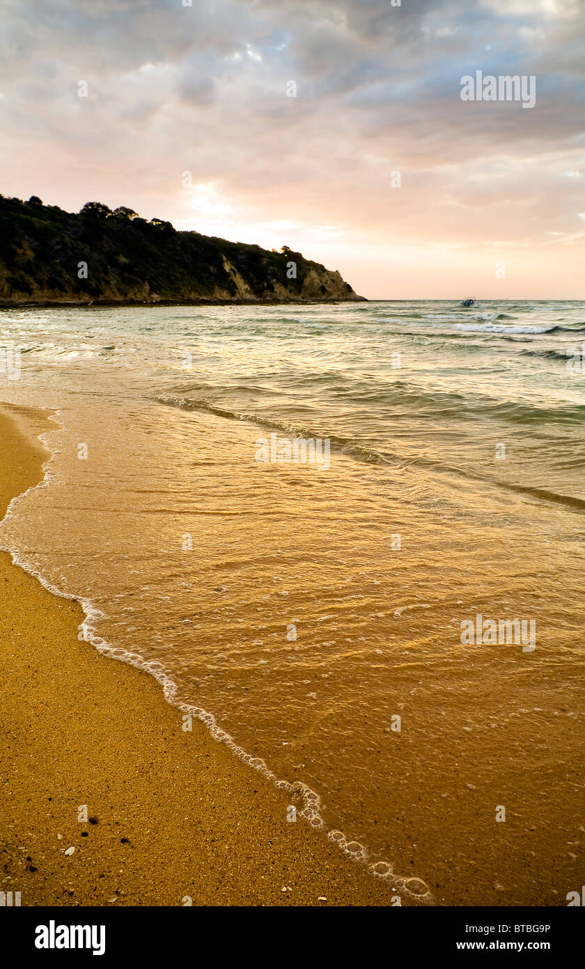 Perfect beach with lapping waves at sunset and a head-land rising up ...