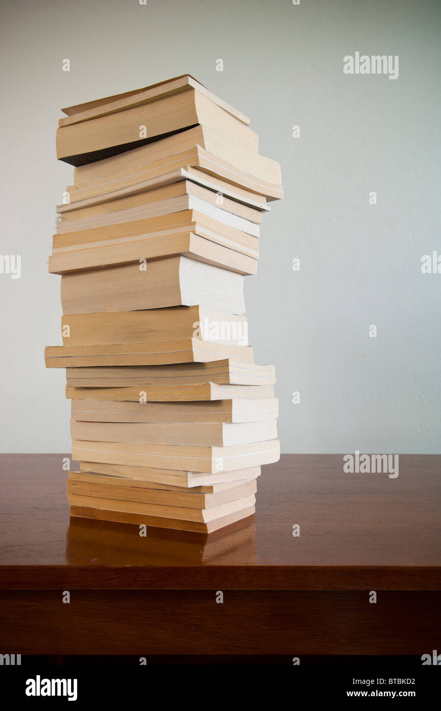 A large pile of books sits on a timber desktop with blank space behind ...
