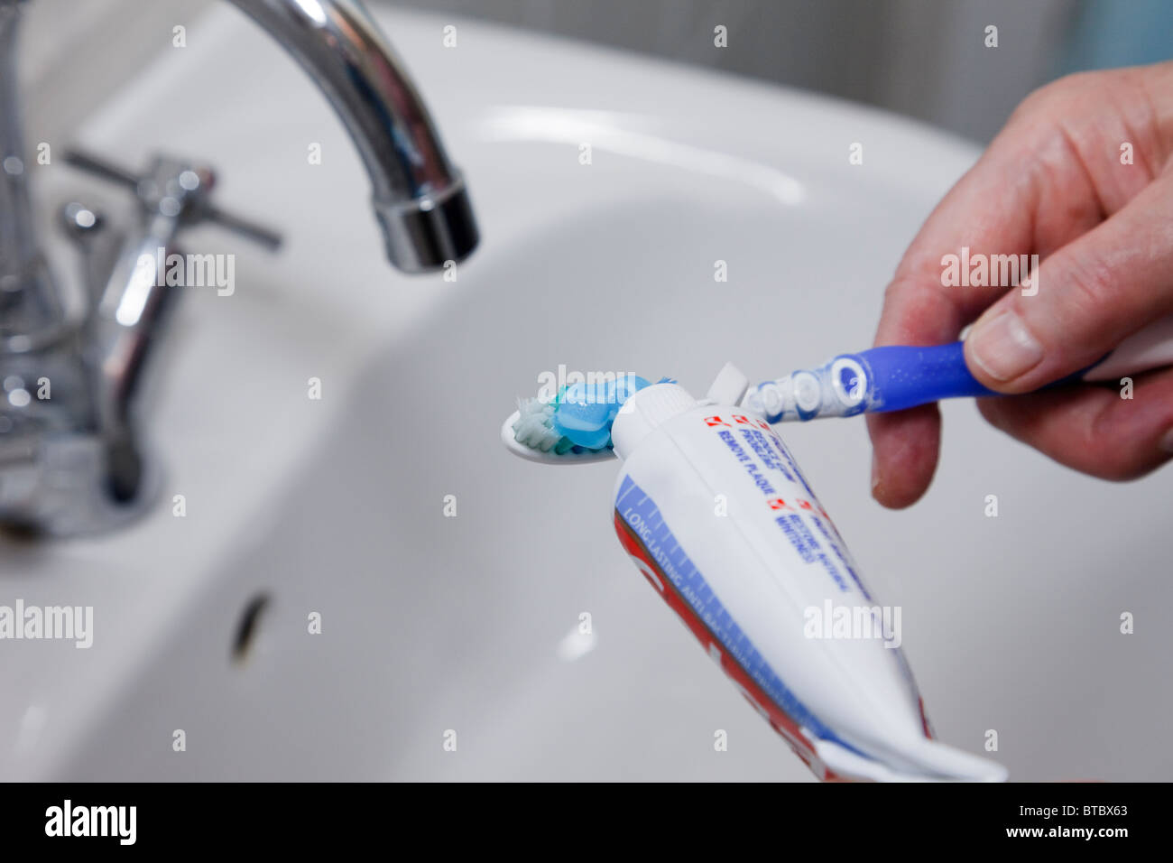 Close-up of a person putting toothpaste on to a toothbrush over a ...