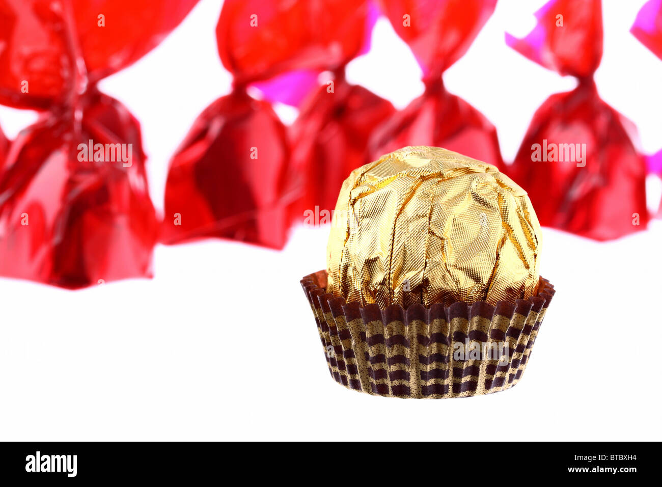 Golden bonbon in front of red luxury sweets isolated on white Stock ...