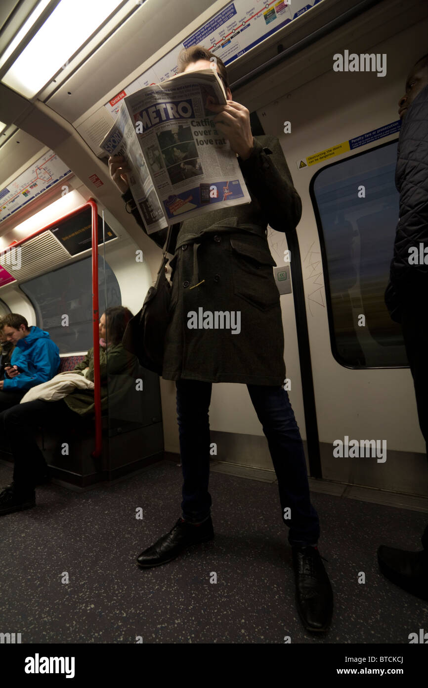 Metro free newspaper reader standing by doors on London underground ...