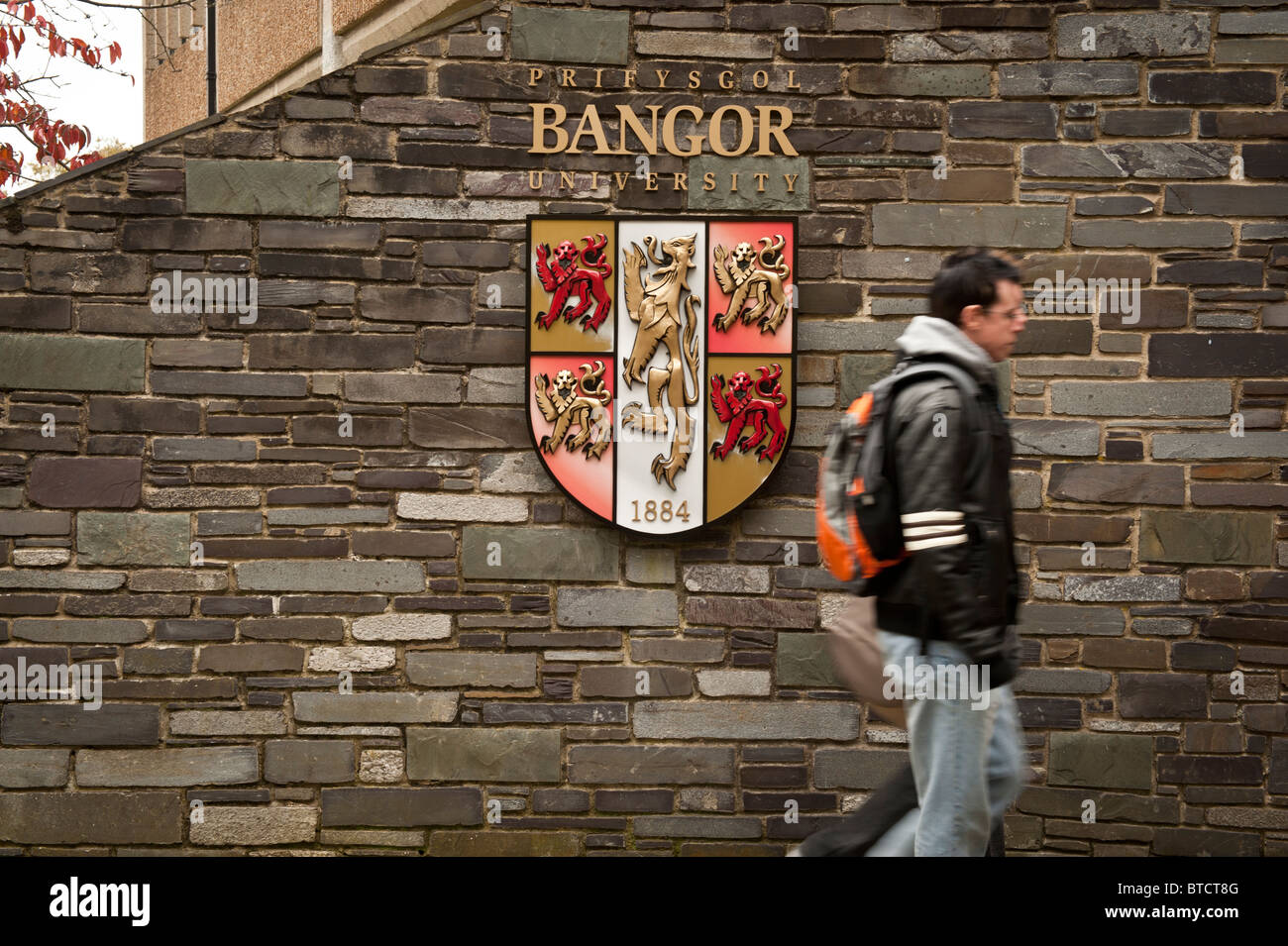 a student walking past the crest shield logo of Bangor University ...