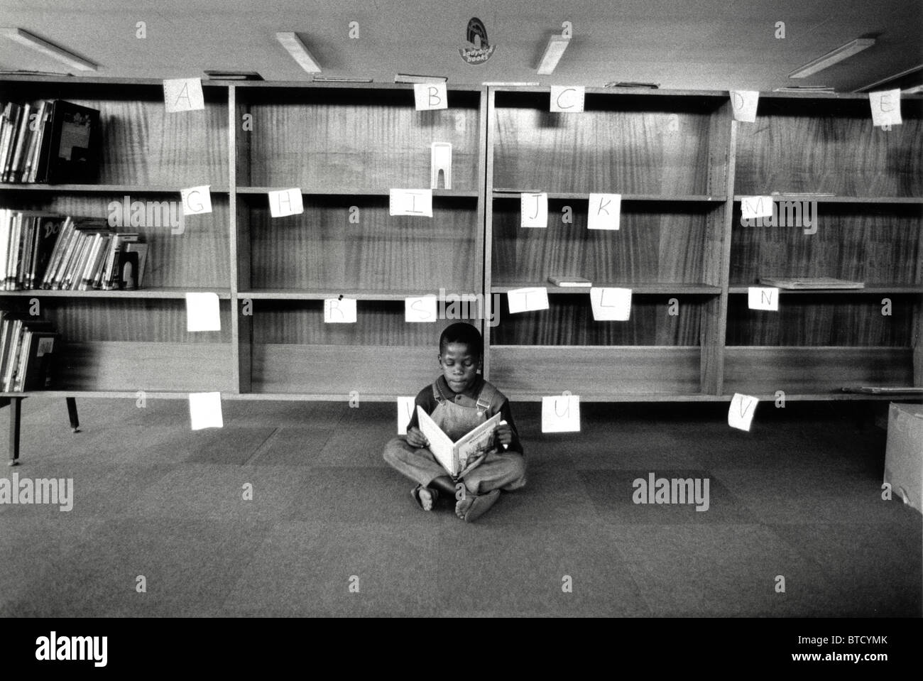 A little boy in front of the almost empty shelves of the library of his ...