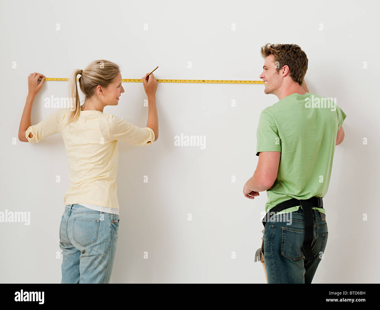 Young couple using measuring tape on wall Stock Photo - Alamy