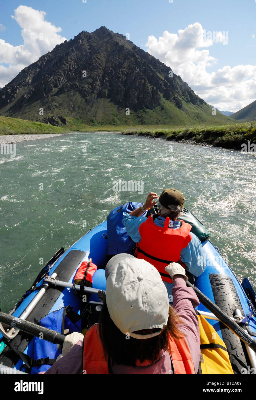 Two rafters rowing through the Kongakut River on a sunny day with ...