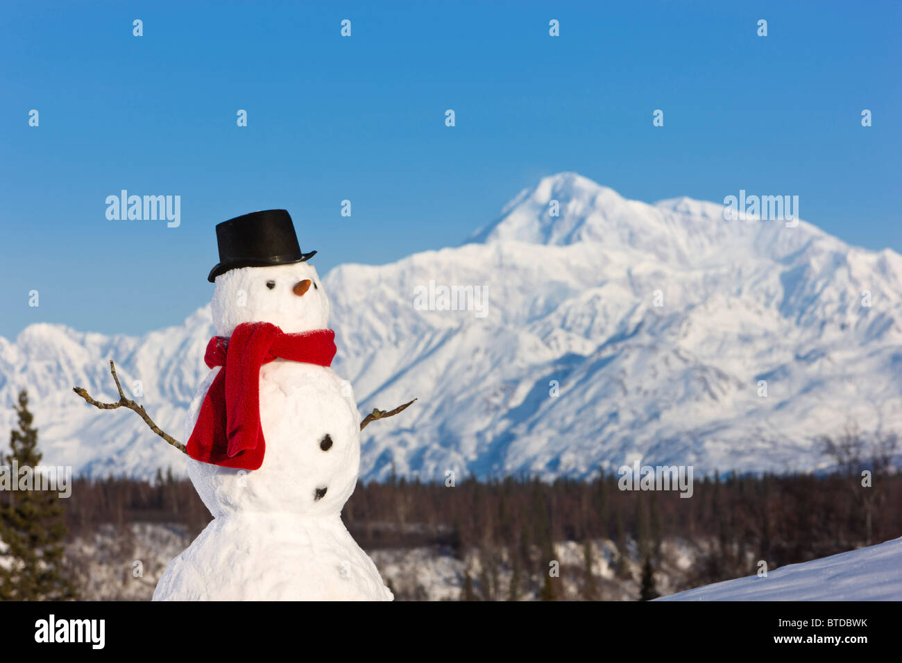 Snowman red scarf and black top hat sitting on a hillside with Mount ...