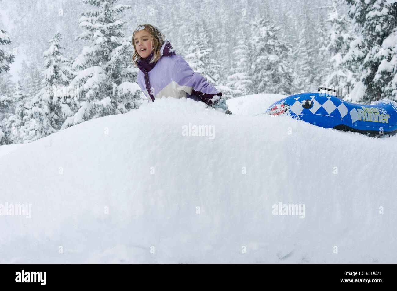 Young girl peers over the steep ledge of snow while sledding after a ...