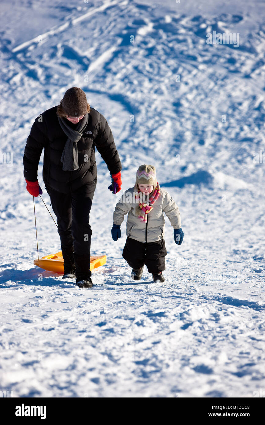 Mother and daughter walking up the sled hill after sleding down it ...