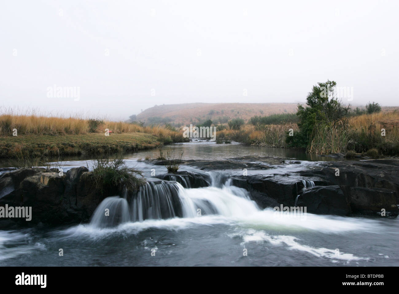 A highveld stream flowing rapidly over rocks and creating a small ...