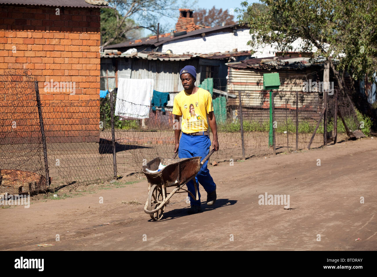 A man pushing a wheelbarrow on a street in the township of Boipatong ...