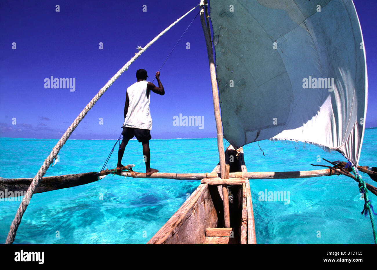 Man balancing on a cross beam and sailing a dhow boat through shallow ...