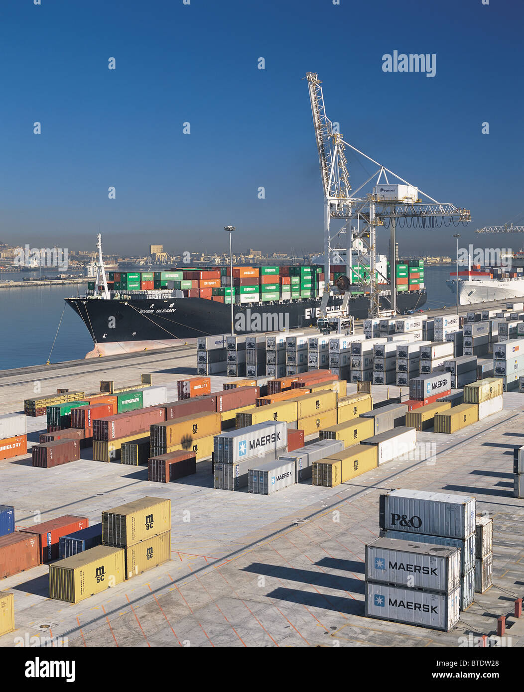 A container ship waits along the wharf while it is being loaded with ...
