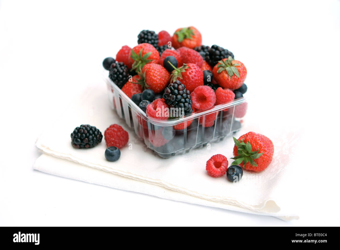 A variety of berries in a plastic carton and loose on a white napkin ...