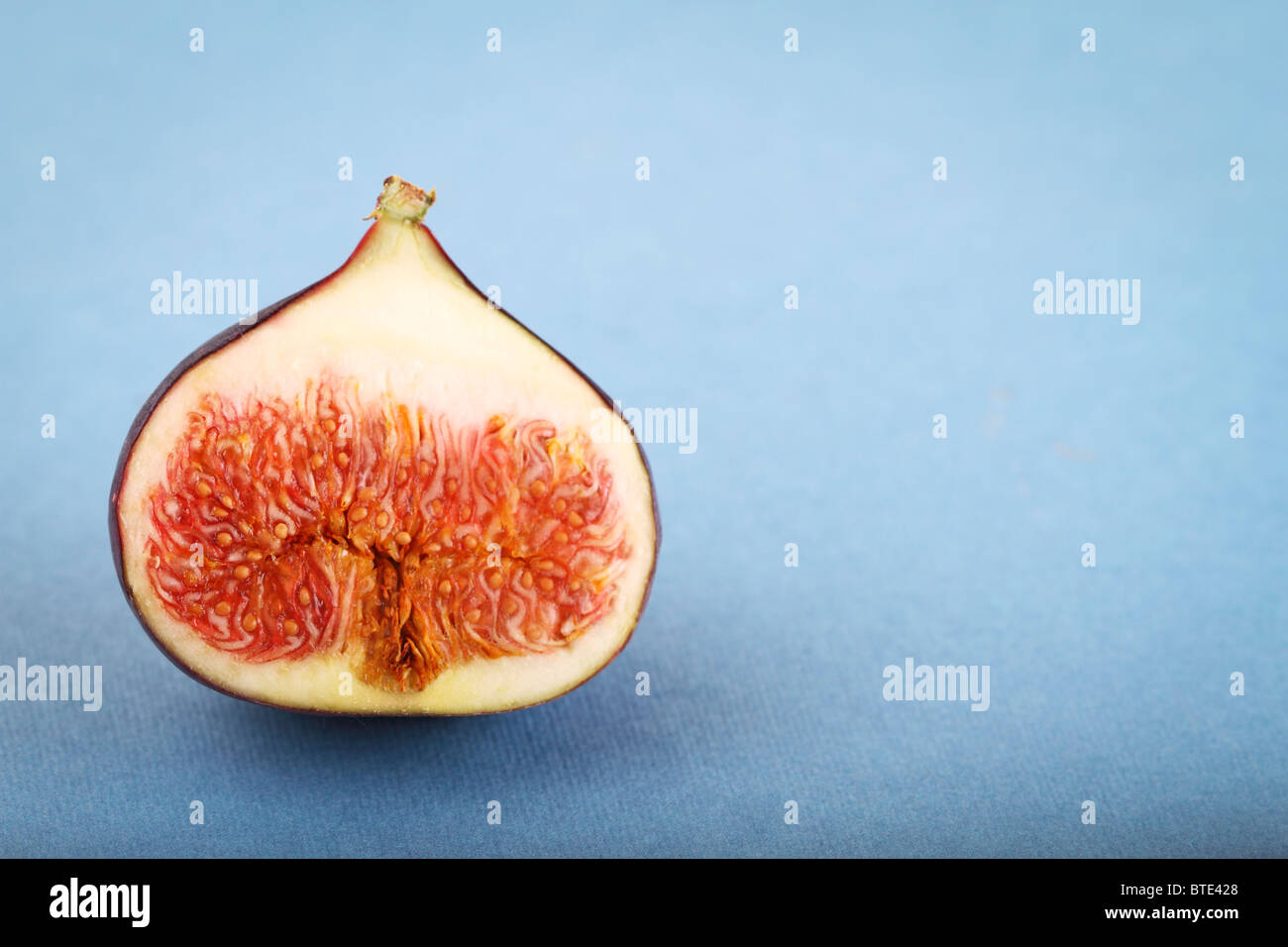 One halved fig on the blue background Stock Photo - Alamy