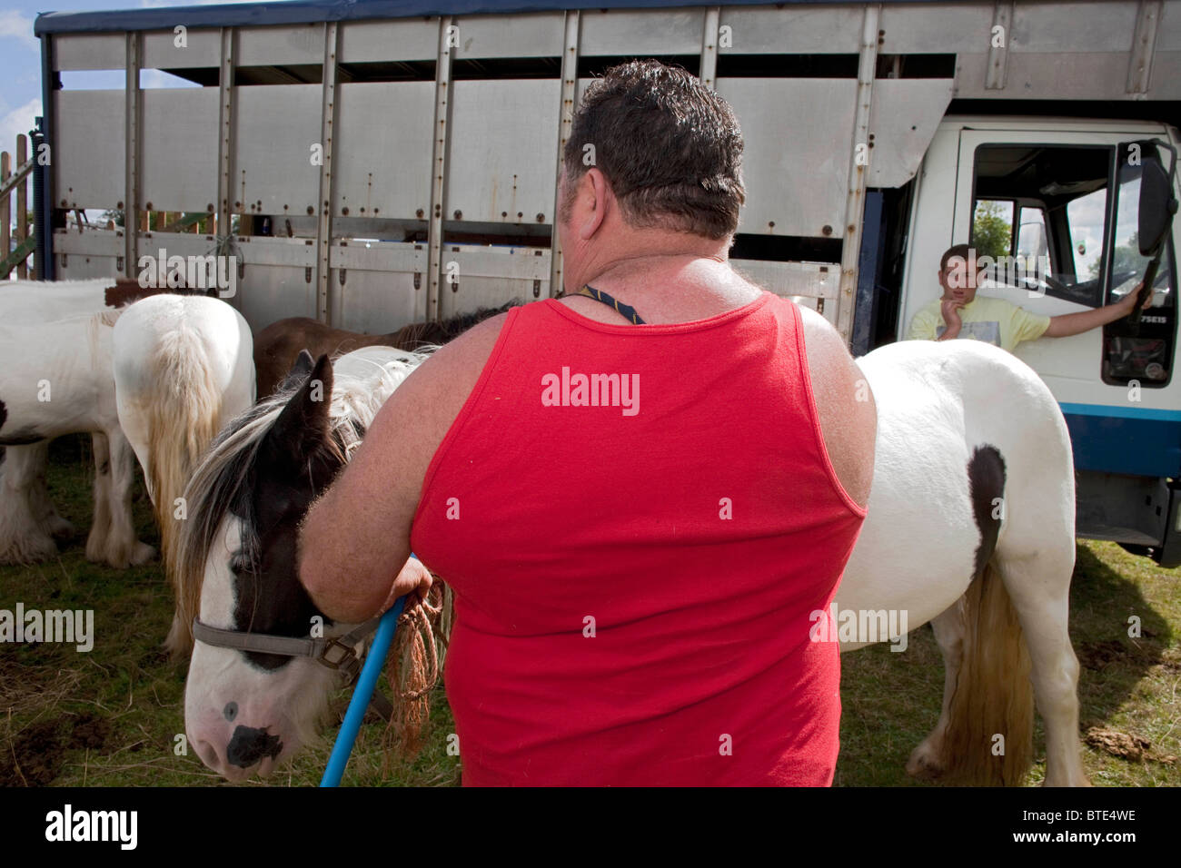 A large strong gypsy man wearing a red vest, stands with his back to us ...
