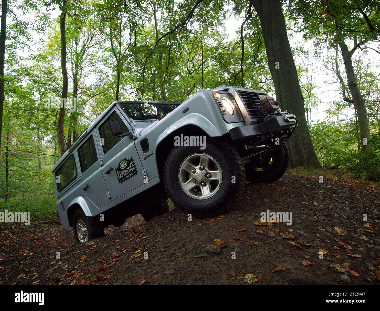 Silver Land Rover Defender driving up a steep and slippery hill Domaine ...